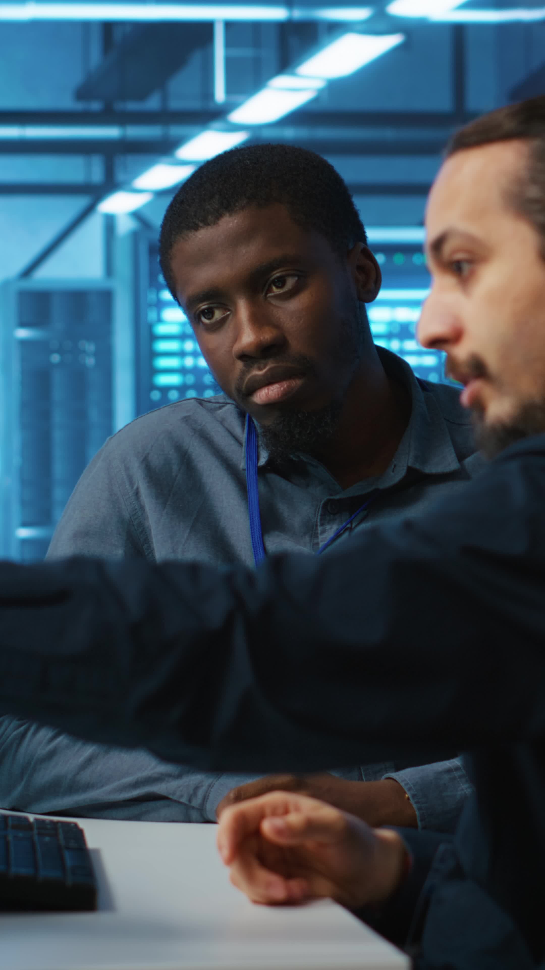 Vertical Multiracial engineers programming in high tech facility with server rows providing ...