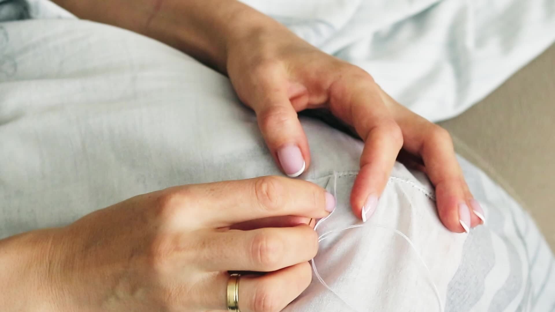 Footage of the woman with beautiful hands stitching up or patching a linen fabric. Craft ...