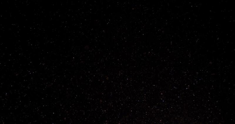 Cinematic purple dust particles floating on black background in slow motion. Atmosphere overlay ...