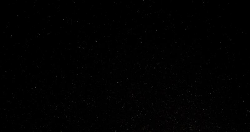 Cinematic dust particles floating on black background in slow motion. Atmosphere overlay. Filmed ...