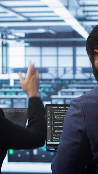 Vertical Teamworking programmers in data center overseeing server operations using laptop and ...