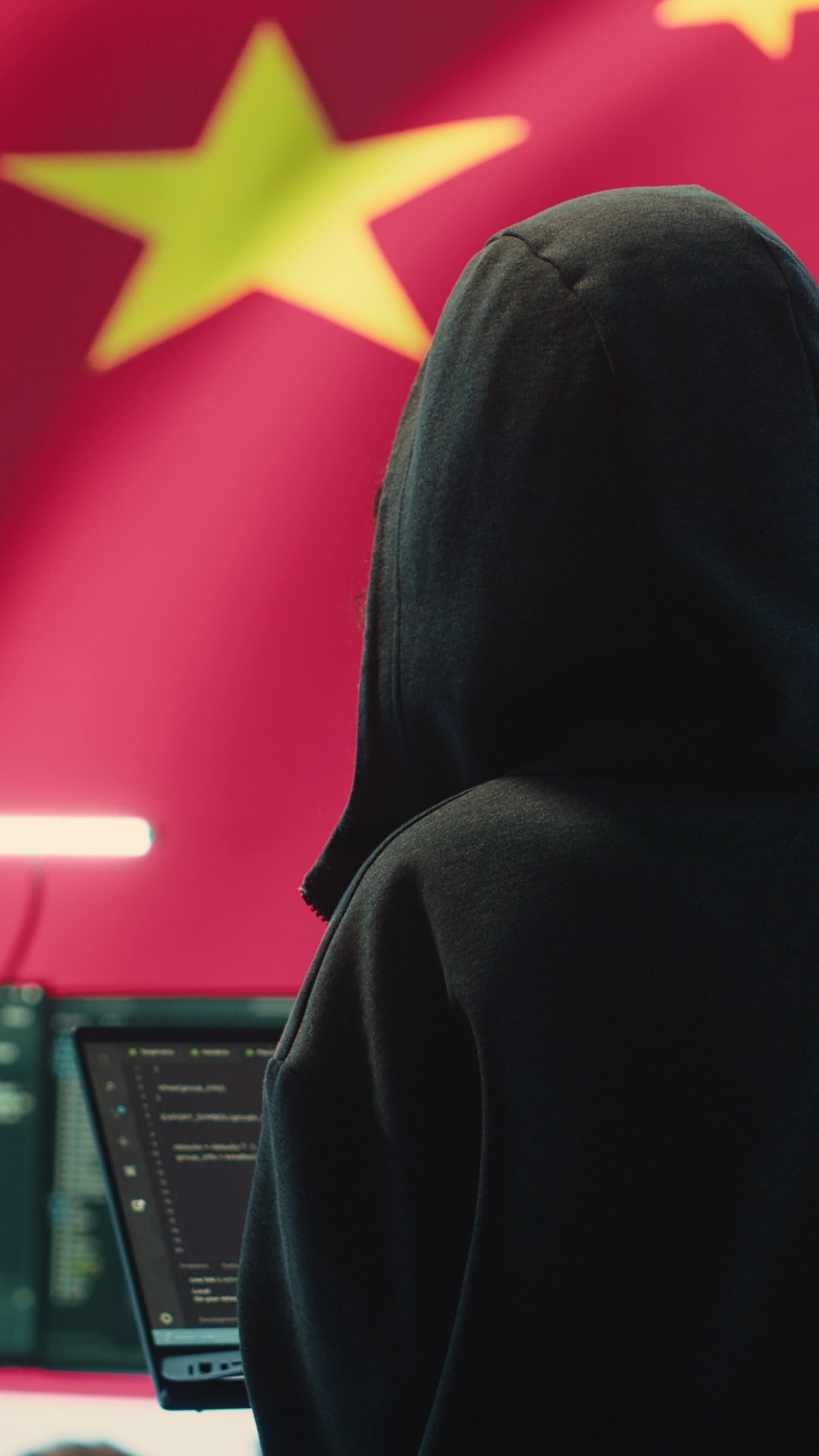 Vertical Chinese Hacker Working In Governmental Hacking Room With Chinese Flag On A Big Screen
