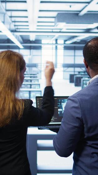 Vertical Teamworking Programmers In Data Center Overseeing Server Operations Using Laptop And