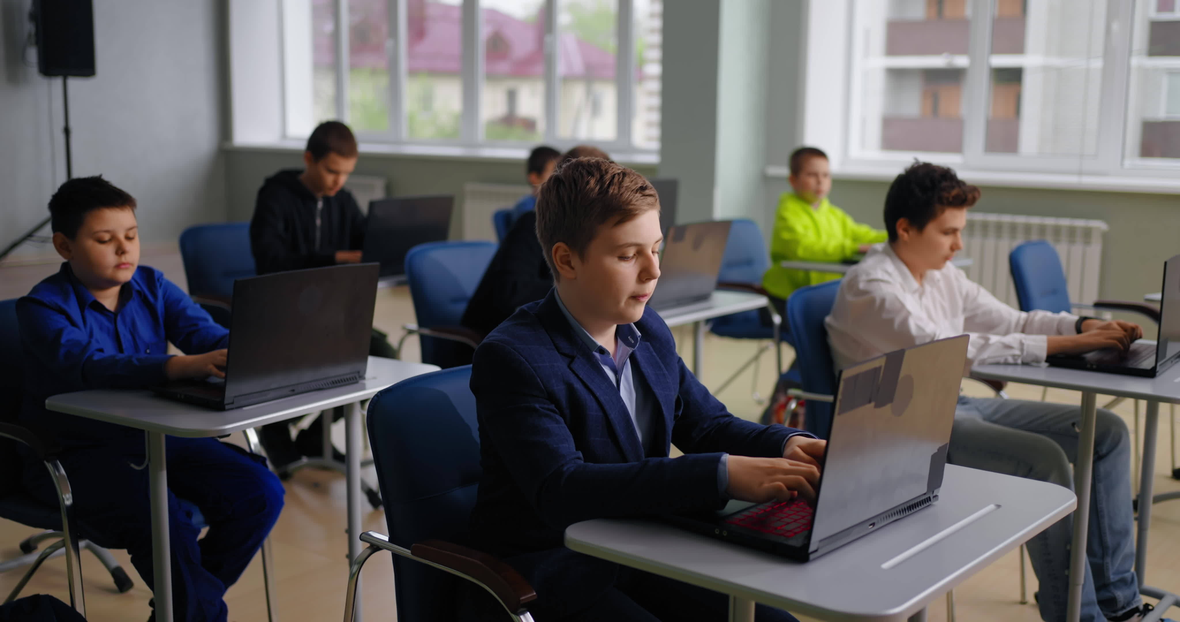 Diverse Teen Boys Sitting At Tables With Modern Laptops In Computer ...