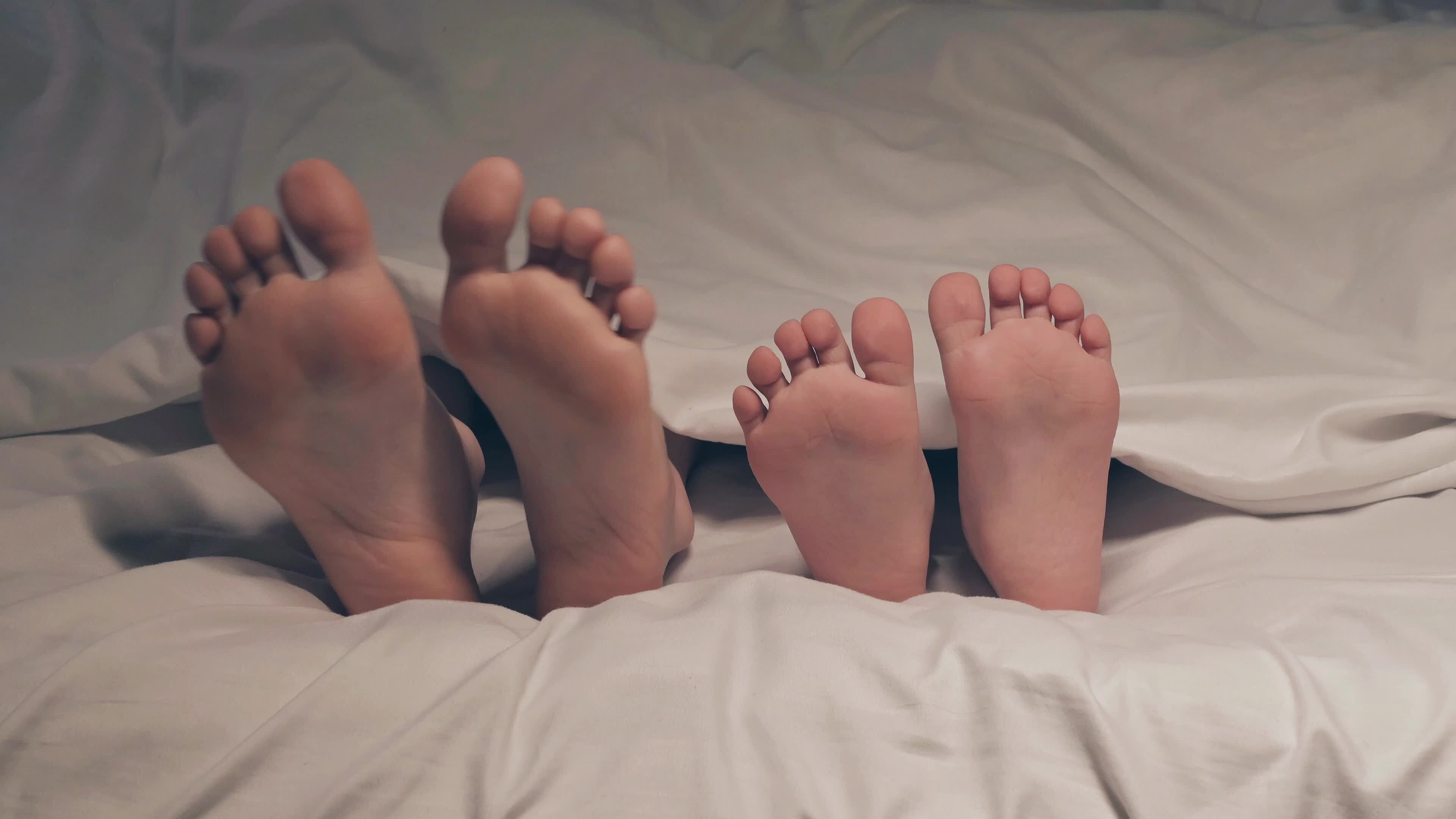 dancing legs of boy son child and mother female foot lie under the blanket on sheet in the ...