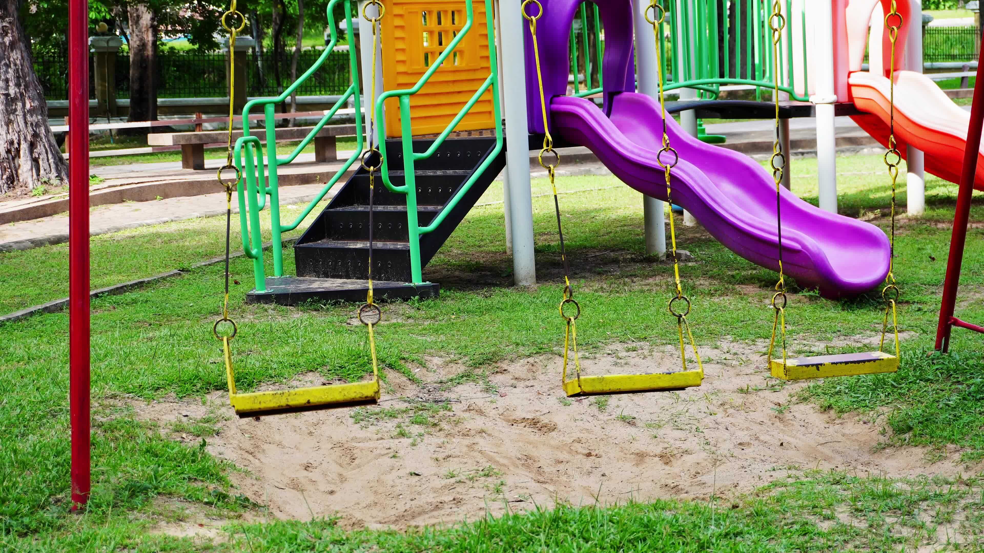 A colorful playground slide and swing on sandy park grounds for ...