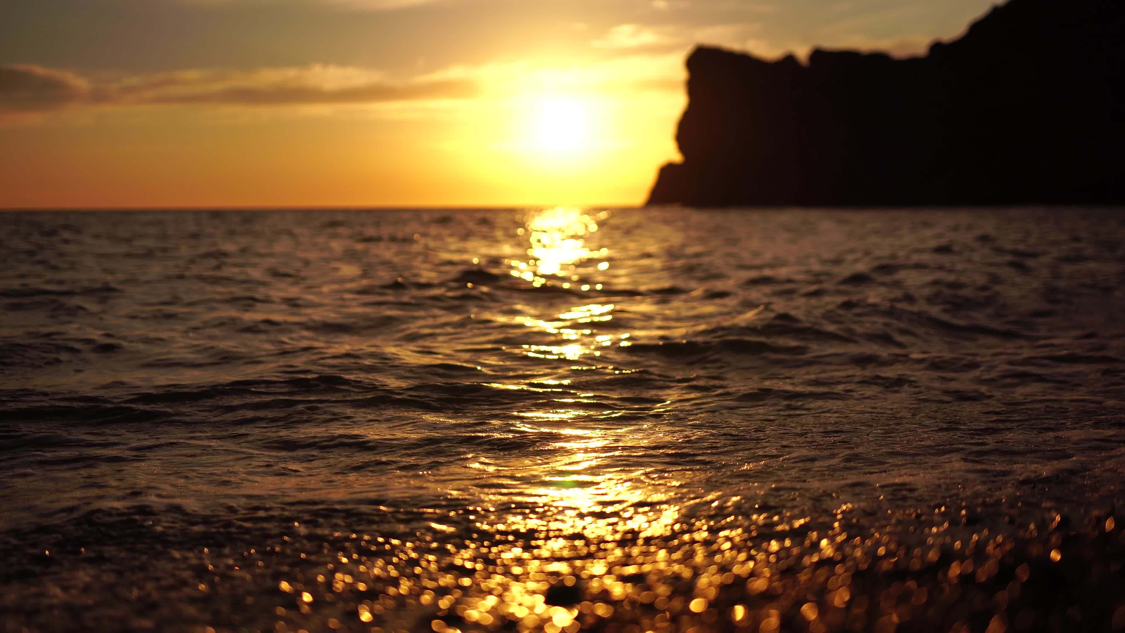 Bright sea sunset. The waves crash into the rock, lit by the warm ...