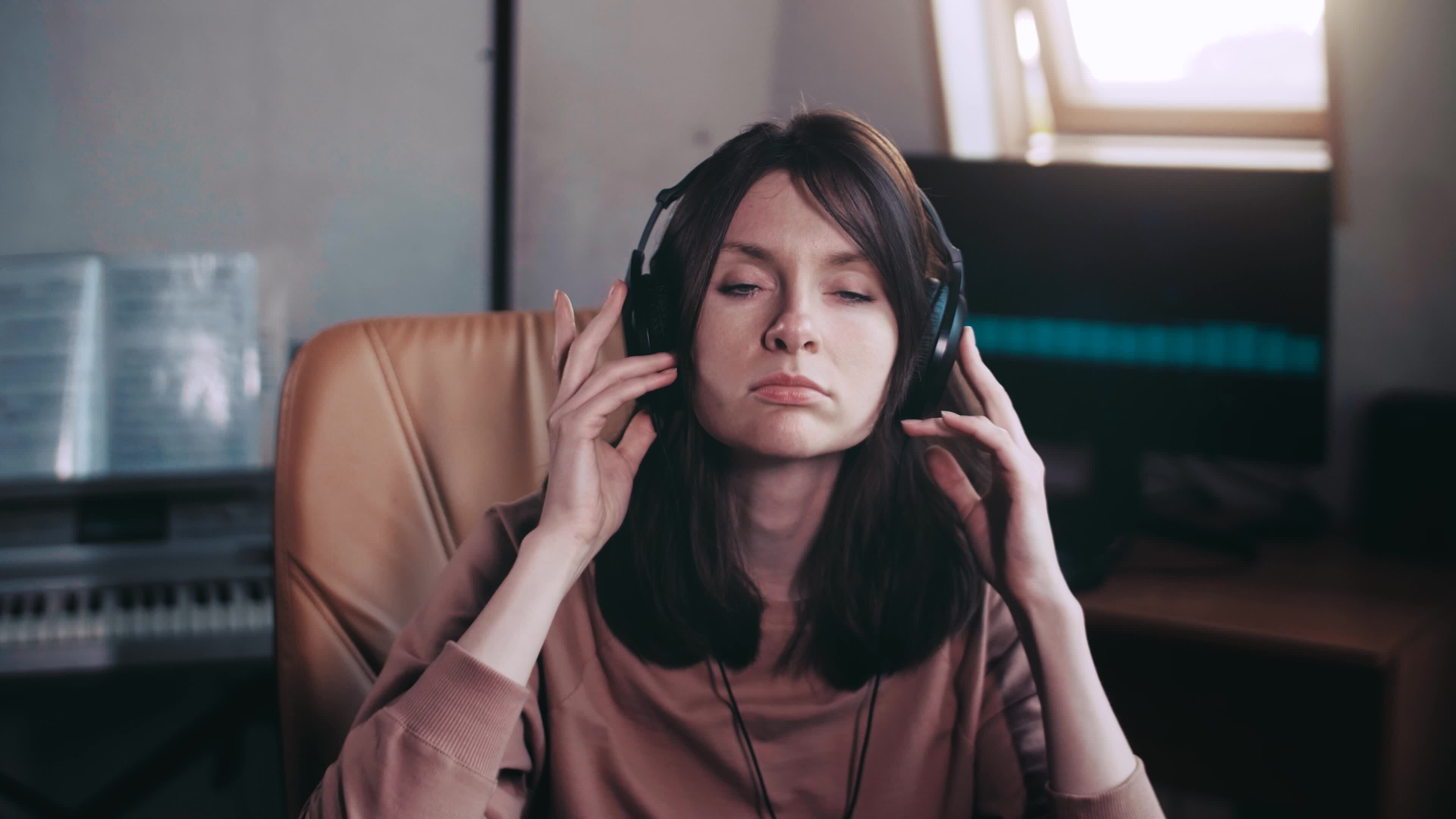 A beautiful girl with headphones listens to music in a chair at the ...