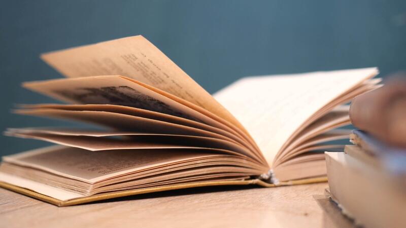 An open book with its pages gently turning rests on a wooden table in ...