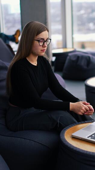young woman wearing eyeglasses working on laptop computer Vertical ...