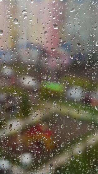 Raindrops on glass window. Water drops falling down on window pane in a rainy weather on city ...