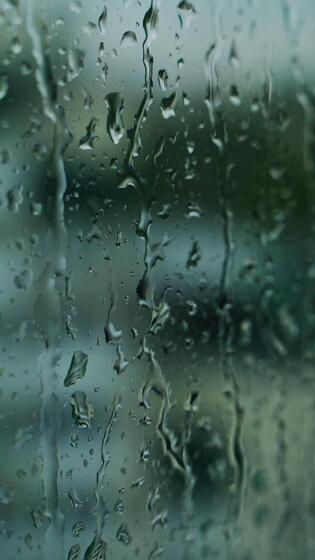 Falling drops on glass. Wet window on blur background. Rain drops running down the window ...