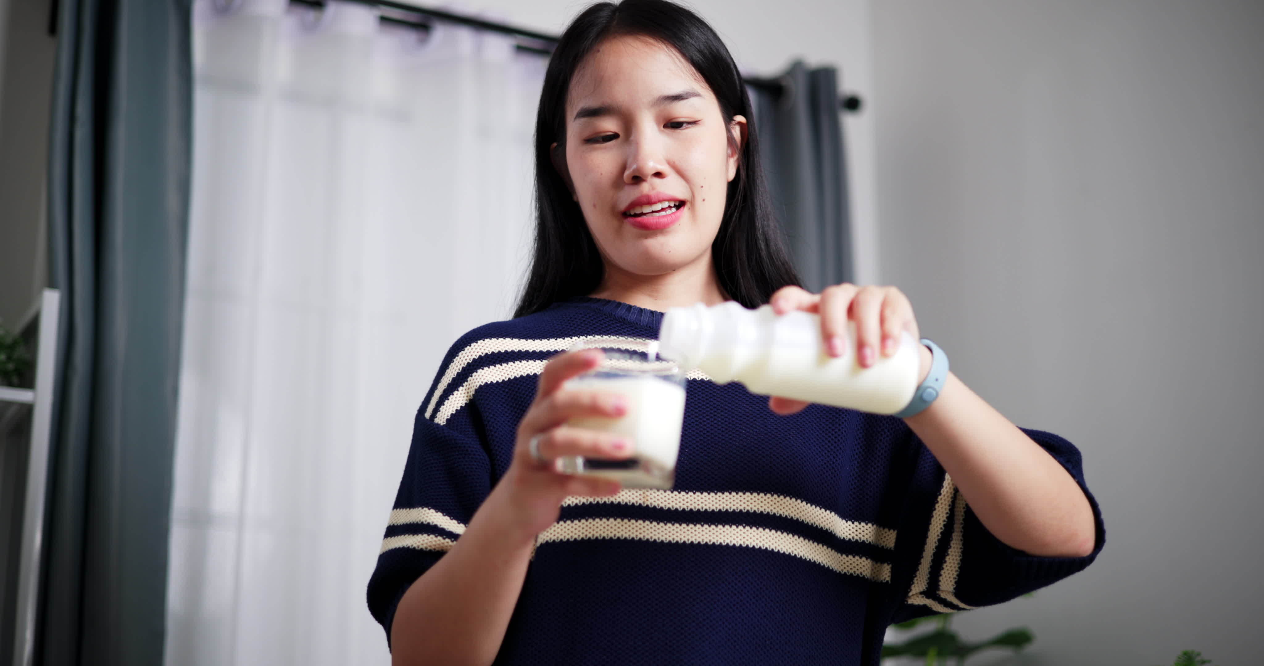 portátil tomada, jovem ásia mulher em pé derramando leite para dentro uma bebendo vidro pronto ...