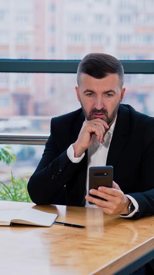 Thoughtful businessman focused on the screen of his smartphone. Busy man scrolling information ...