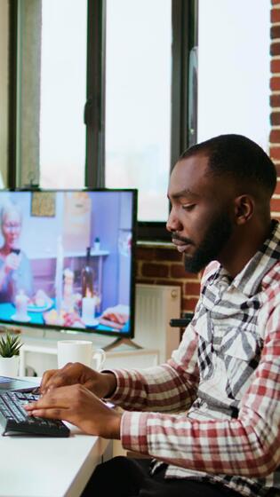 Vertical Male coder works from home typing code on a laptop in a modern living room. African ...