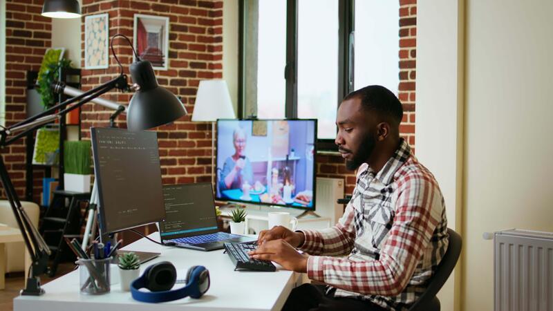 Male Coder Works From Home Typing Code On A Laptop In A Modern Living Room African American It