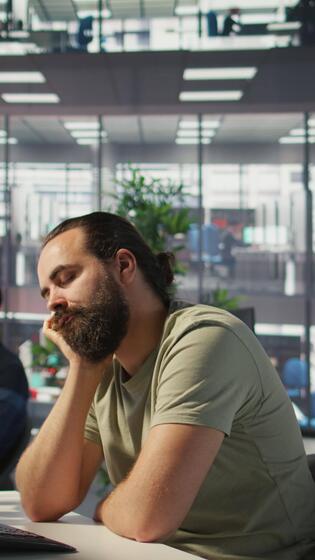 Vertical Fatigued software engineer caught asleep at desk by manager while developing artificial ...
