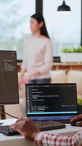 Vertical Male coder works from home typing code on a laptop in a modern living room. African ...