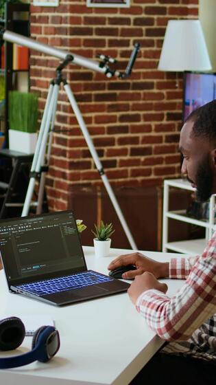 Vertical Male programmer developing an app on his laptop and working remotely. Home office setup ...