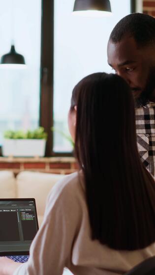 Vertical Interracial creative team programing code on a laptop and debugging, using digital ...