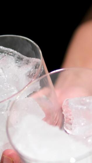 Bartender adds ice cubes into glass. slow motion, making cocktail at bar counter, Vertical ...