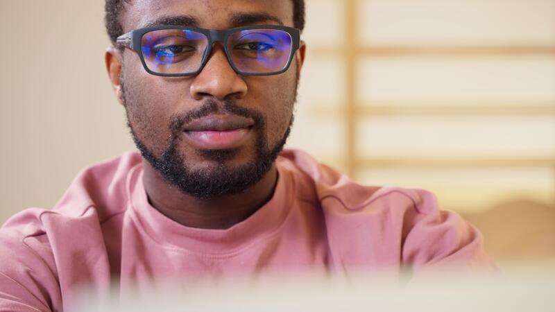portrait of focused black man with eyeglasses working with computer ...