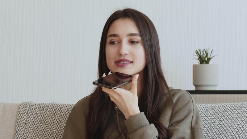 Jeune fille en utilisant voix reconnaissance sur téléphone à record message, séance sur canapé à ...