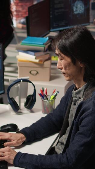 Vertical Senior programmer in AI startup office putting on headphones, refining machine learning ...