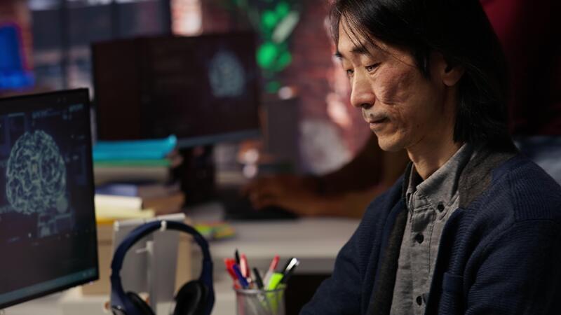 Senior programmer in AI startup office putting on headphones, refining machine learning models ...