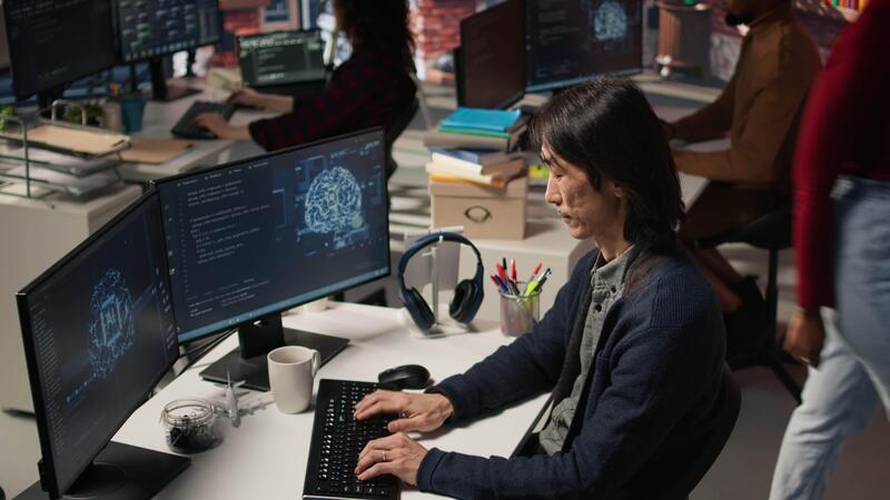 Senior programmer in AI startup office putting on headphones, refining machine learning models ...