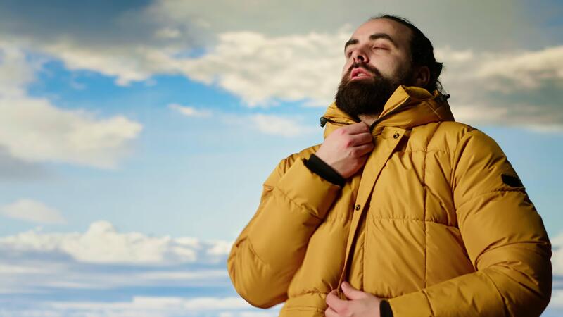 Mountain hiker zipping his jacket after climbing to the top with a vast landscape of peaks and ...