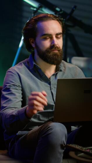 Vertical Man typing on laptop keyboard in neon lit apartment, sitting ...