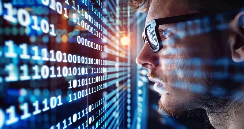 A young male IT specialist looks at a digital board with binary program ...