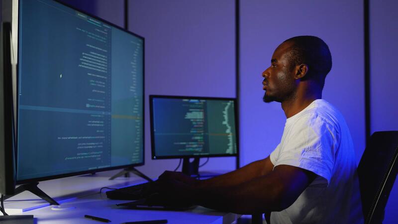 African American programmer coding on multiple screens at night ...