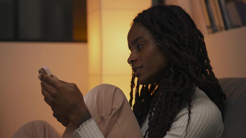 Side profile portrait of a young African American woman sitting on a couch, focused and ...