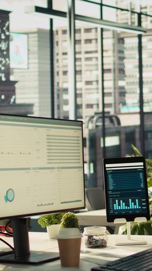 Vertical Computer screen on office desk displaying financial charts of company profits ...
