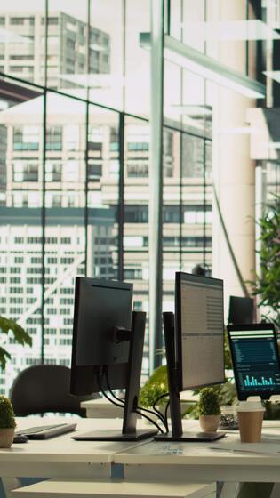 Vertical Modern office workspace desk with computer monitors displaying graphs, charts and data ...