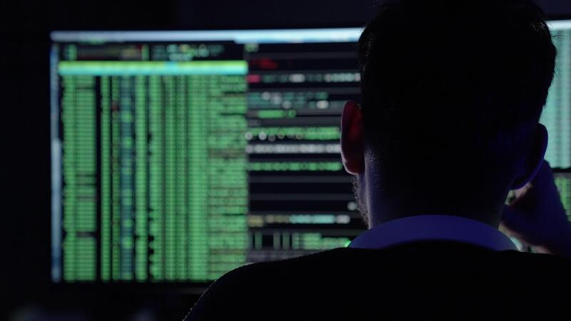 Young man working late at night on programming tasks with multiple screens displaying code data ...
