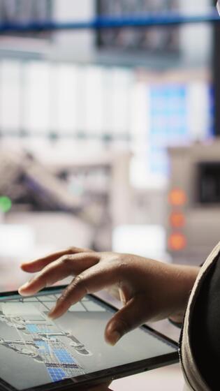 Vertical Close up of technician using tablet CAD app to design smart factory layouts. Specialist ...