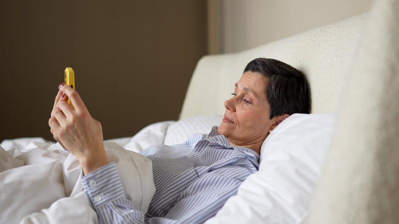 Calm drowsy apathetic woman in bed scrolling smartphone. Social media check, chat in morning ...