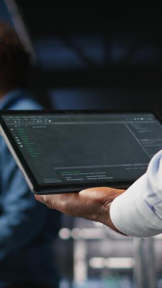 Vertical Close up of data center admin using tablet to reviewing machine learning code ...