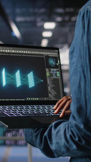 Vertical Close up of admin in data center using laptop to monitor neural network LLM ...