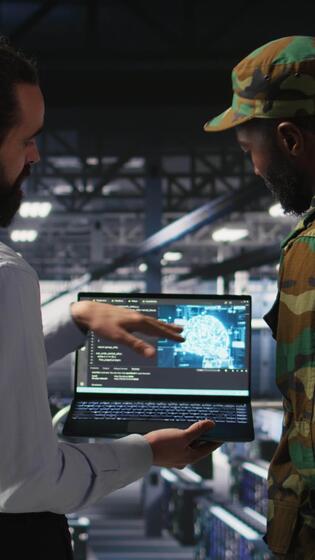 Vertical Military technicians in secure data center use laptop to monitor artificial ...