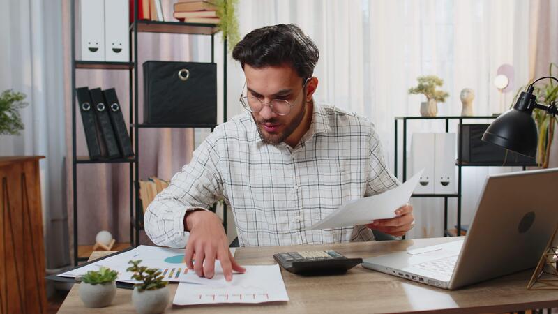 Focused young Indian office worker working with schedules and financial ...
