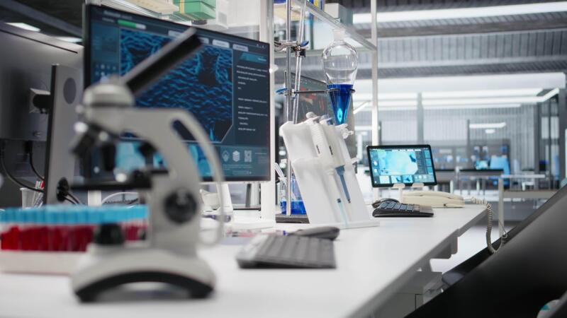 Close up of microscope in lab next to computer monitor displaying DNA ...